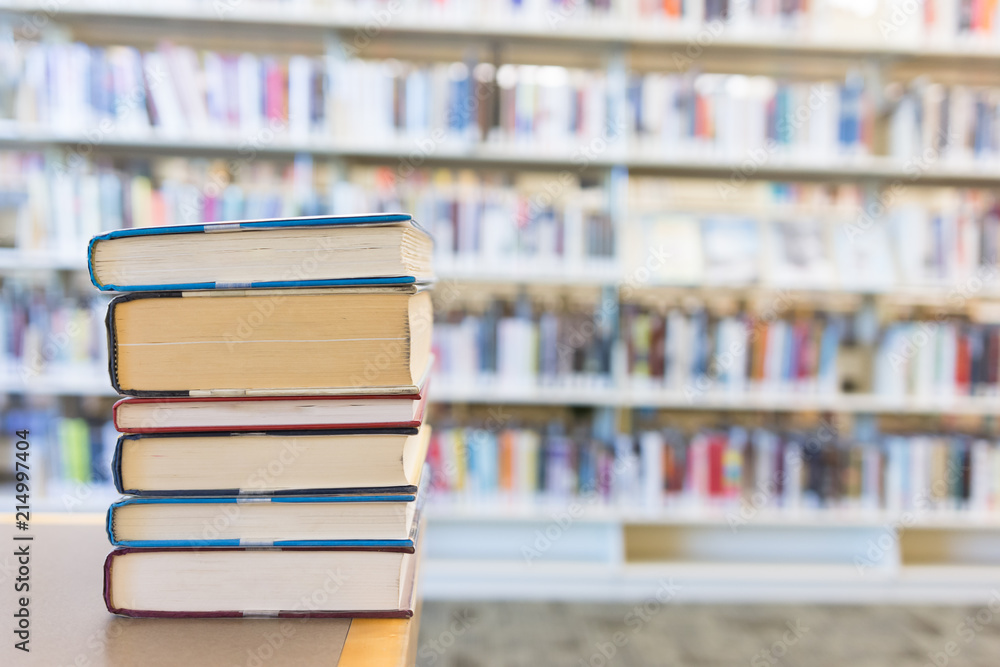 Small stack of various sized books on library desk with shelves of ...