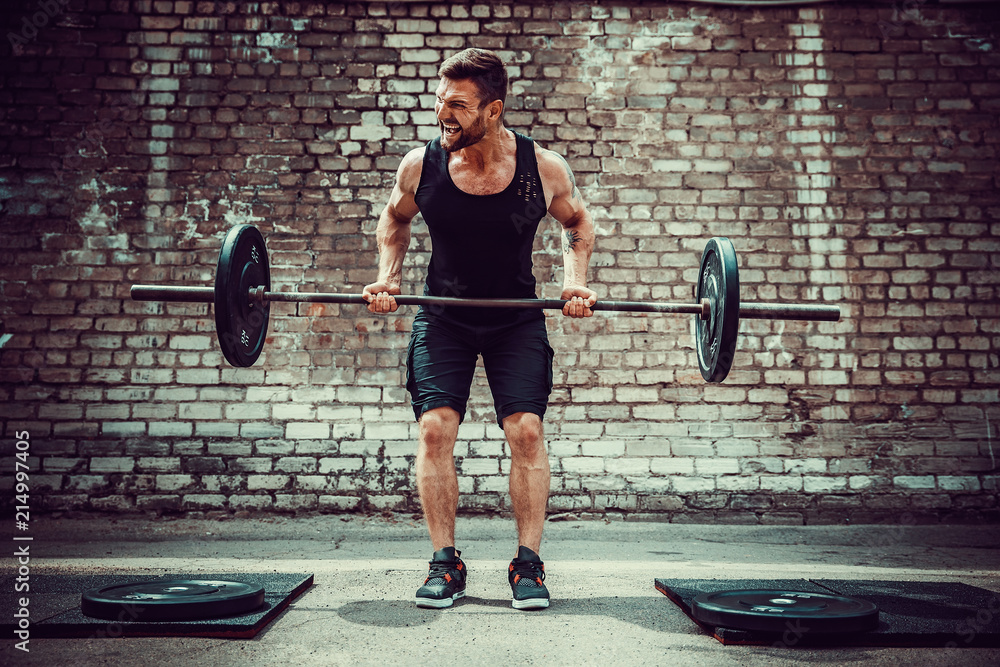 Athletic man working out with a barbell in front of brick wall ...