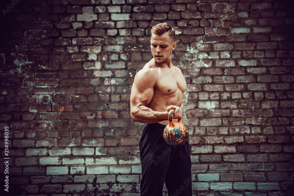 Athletic man working out with a kettlebell in front of brick wall ...