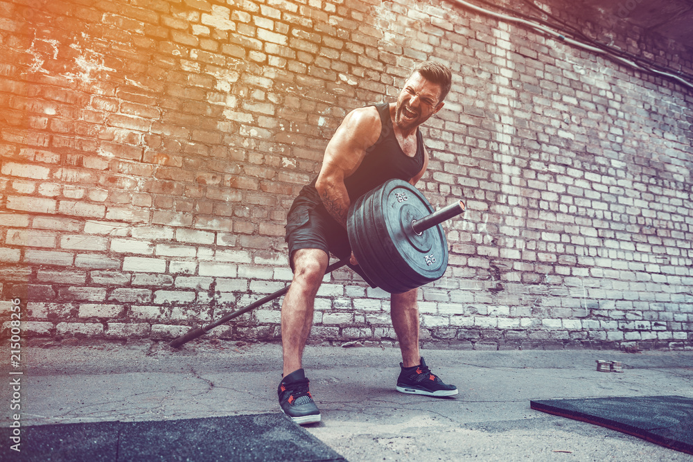 Athletic man working out with a barbell in front of brick wall ...