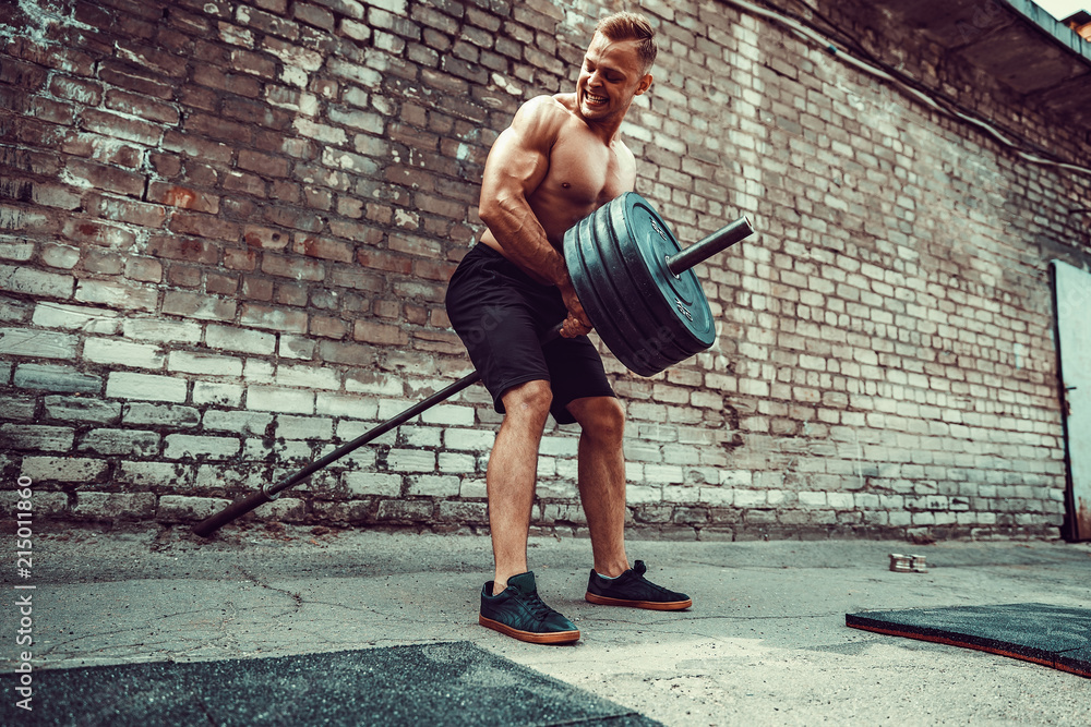Athletic man working out with a barbell in front of brick wall ...
