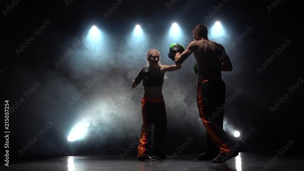 Guy with a girl boxing gloves beating in the ring in the dark, they are ...