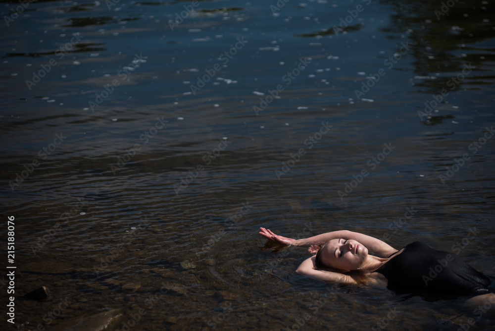 girl lying on her back in the lake. Beautiful woman in a black swimwear ...