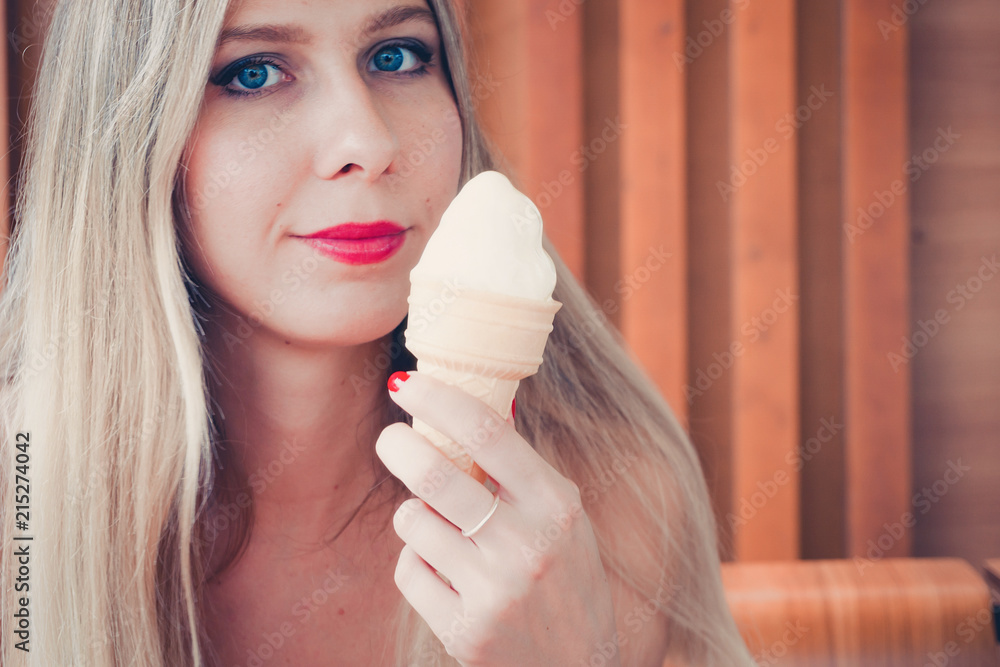 Pretty young girl licks a horn with ice cream on a hot day outdoors. Model chokes with ice cream ...