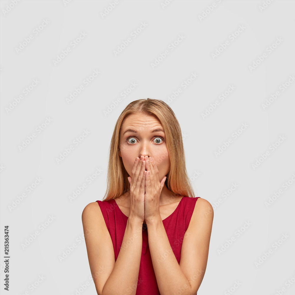 Shocked blonde woman exclaims with terror, covers mouth with hands, has ...