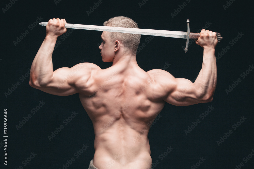 Bodybuilder man posing with a sword isolated on black background ...