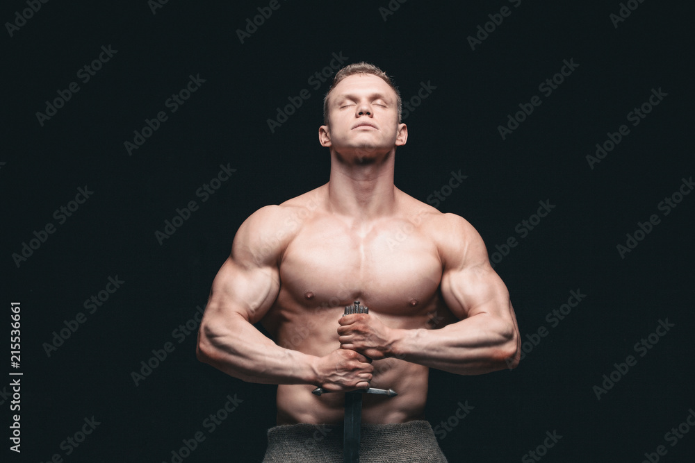 Bodybuilder man posing with a sword isolated on black background ...