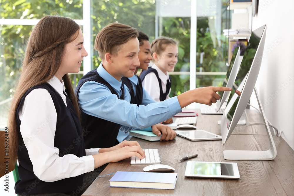 Teenage students in stylish school uniform at desks with computers ...
