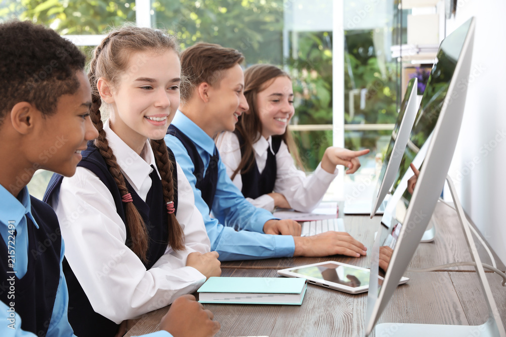 Teenage students in stylish school uniform at desks with computers ...