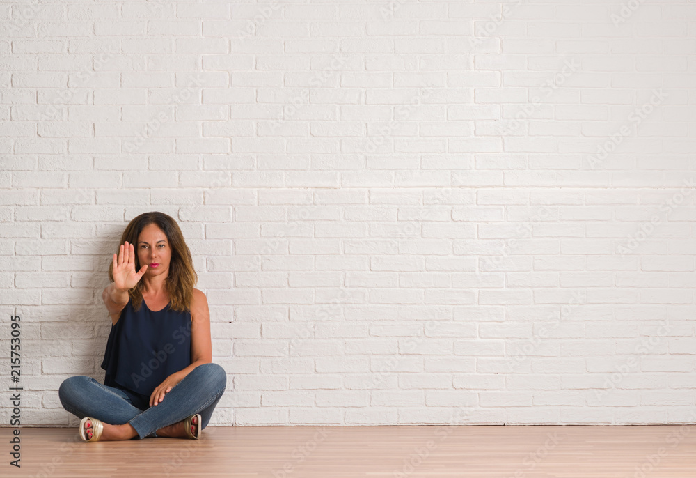 Middle age hispanic woman sitting on the floor over white brick wall ...