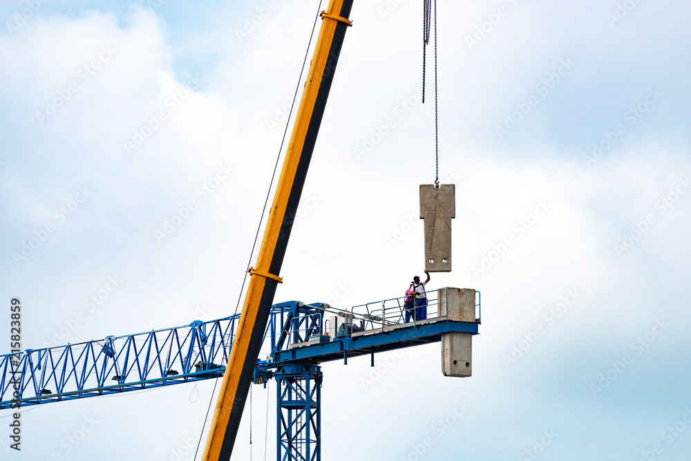 Setting up a blue tower crane in the construction site. Workers are ...