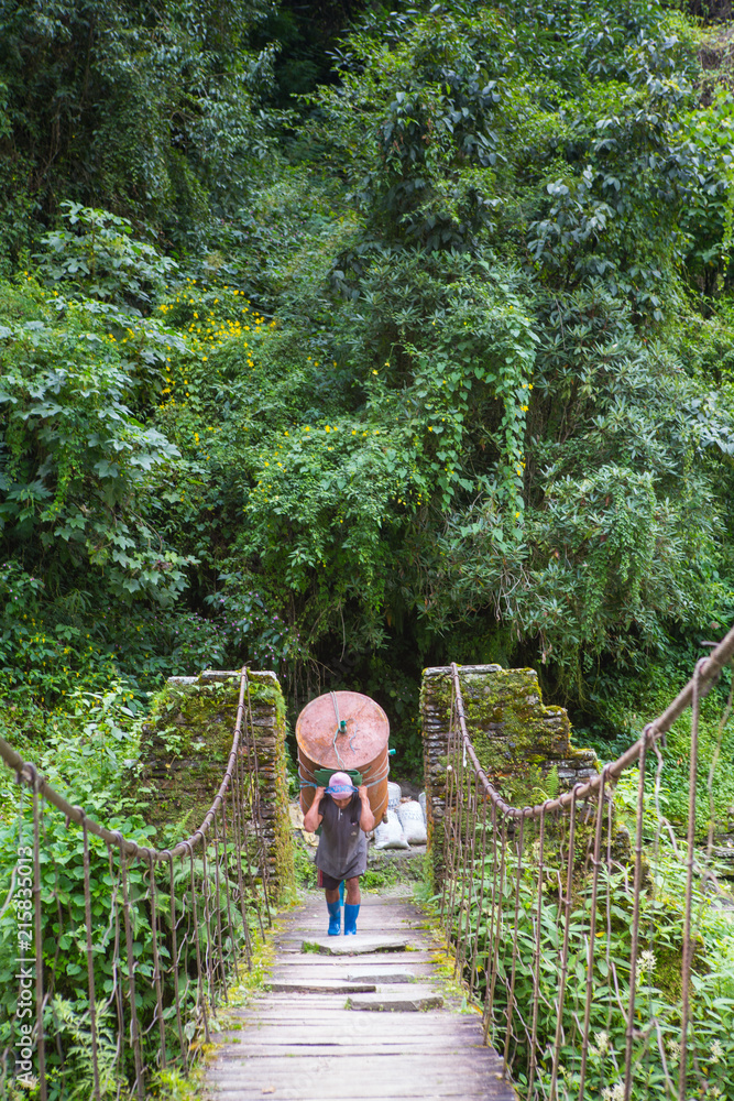 Nepali man hauling heavy metal barrel on his back across bridge in the ...