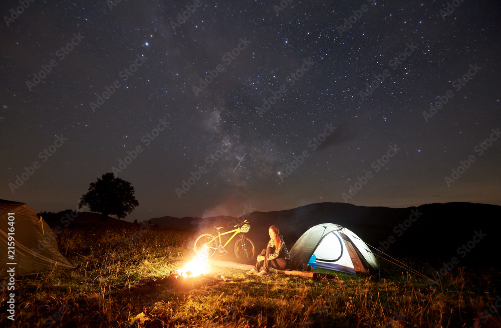 Young woman traveller enjoying at night camping near burning campfire ...