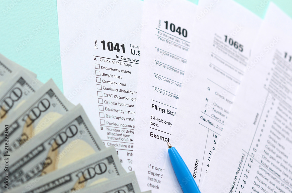 Tax forms lies near hundred dollar bills and blue pen on a light blue ...