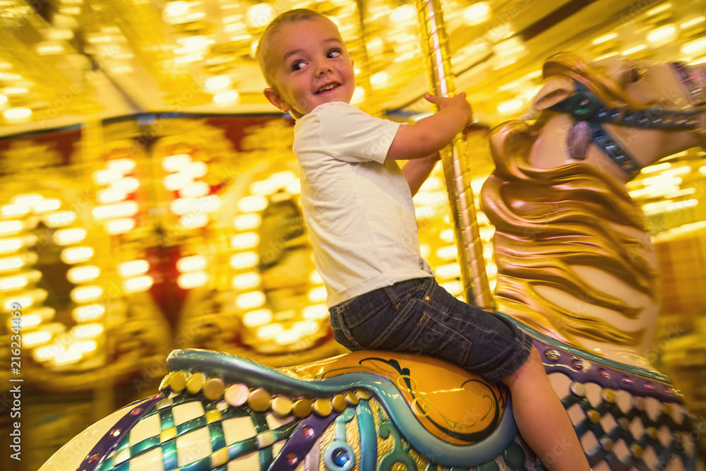 Cute little boy having fun riding a carousel at an amusement park or ...