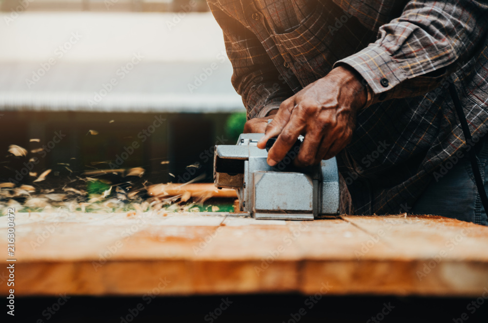 Carpenter with power tools using electric planer on wooden plank in ...