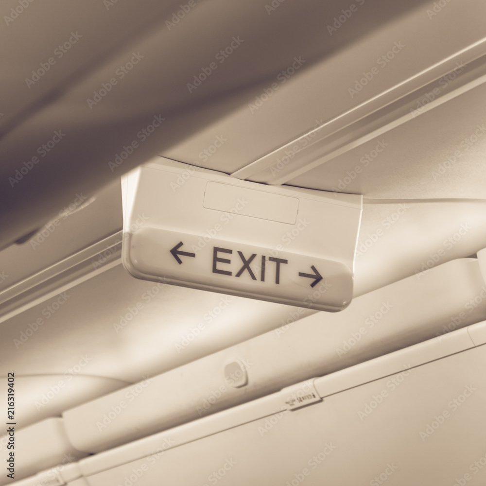 Vintage tone emergency exit sign with red arrow on ceiling of airplane ...