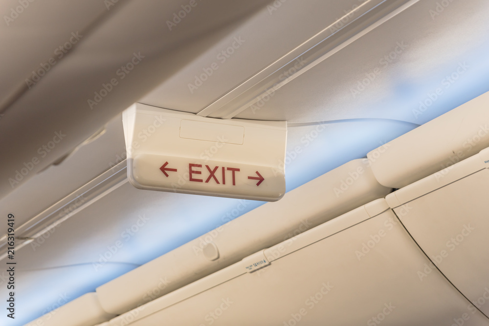 Emergency exit sign with red arrow on ceiling of airplane. Illuminated ...