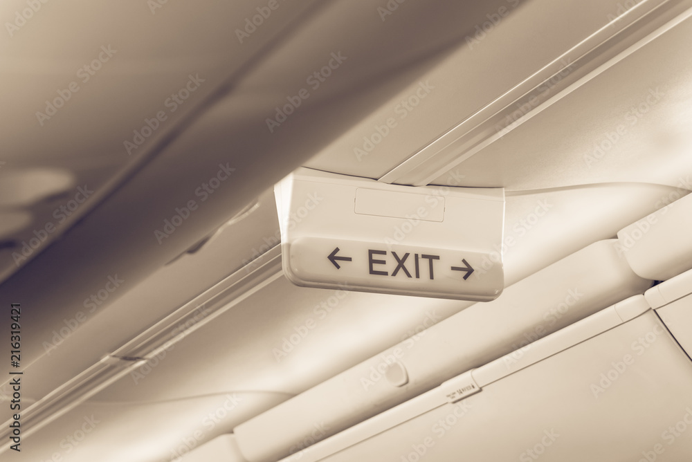 Vintage tone emergency exit sign with red arrow on ceiling of airplane ...