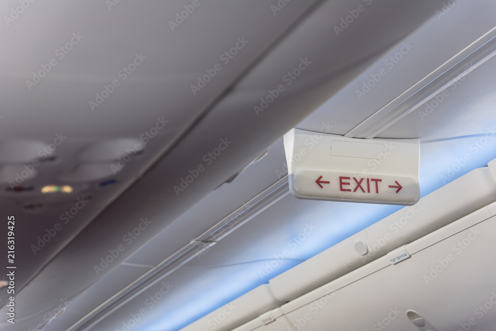 Emergency exit sign with red arrow on ceiling of airplane. Illuminated ...