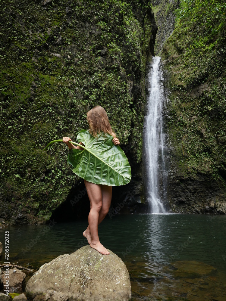 woman covered with big green leaf standing on a rock at a tropical ...