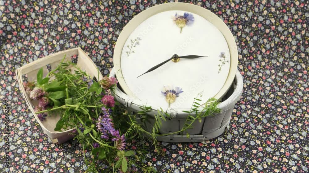 A clock in a blue wicker basket and a small bouquet of wild flowers in ...