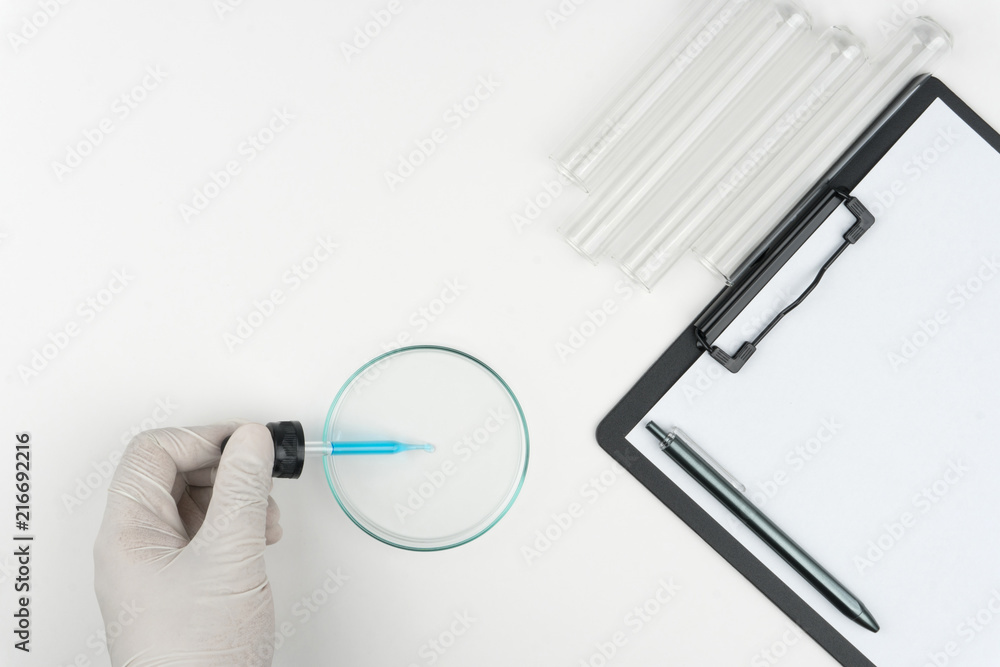 laboratory scene, the scientist holding a blue liquid dropper over the ...