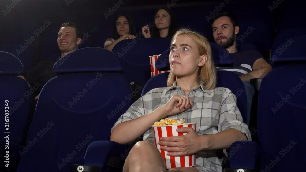 Beautiful young woman eating popcorn at the cinema, enjoying watching ...
