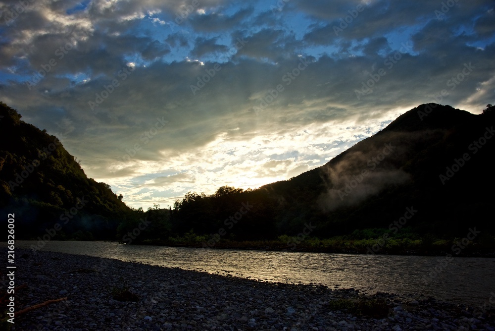 Sunset over mountains. Golden clouds after rain over river valley and ...