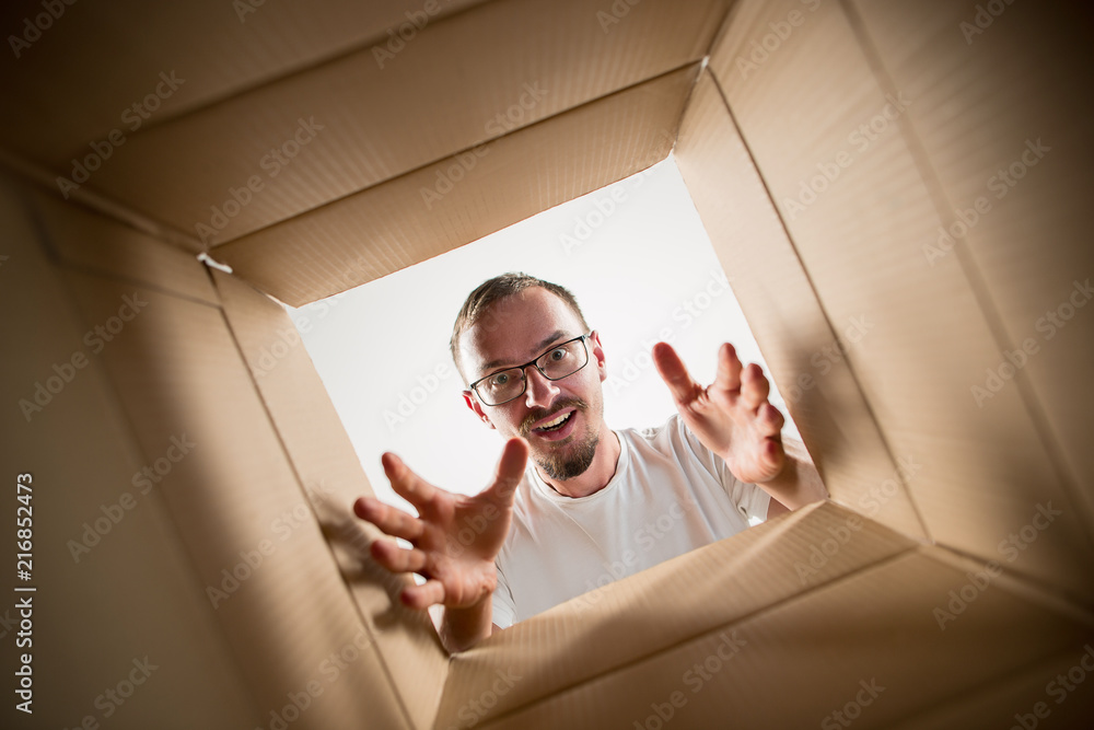 The surprised man unpacking, opening carton box and looking inside. The ...