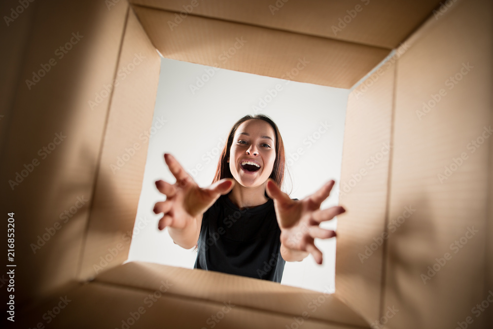 The surprised woman unpacking, opening carton box and looking inside ...
