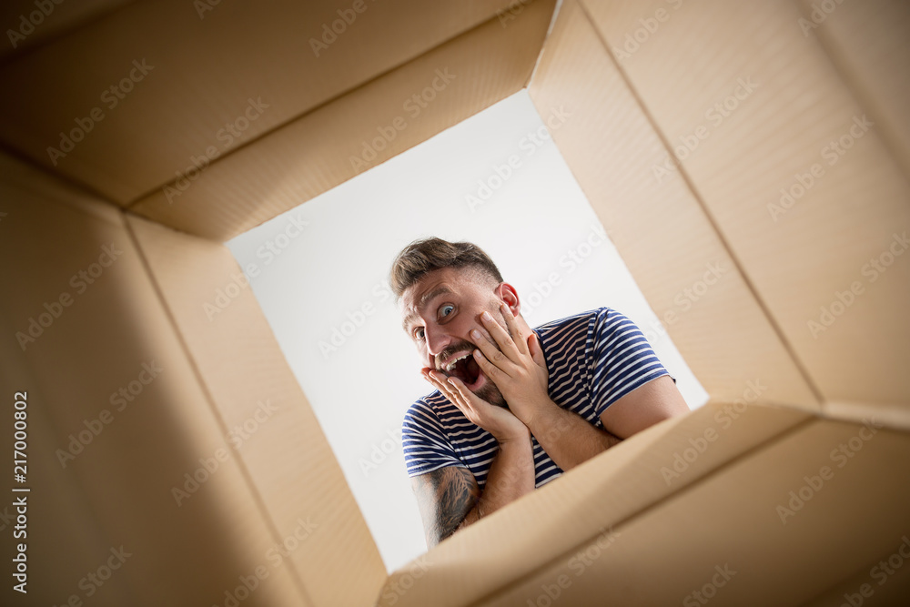 The surprised man unpacking, opening carton box and looking inside. The ...