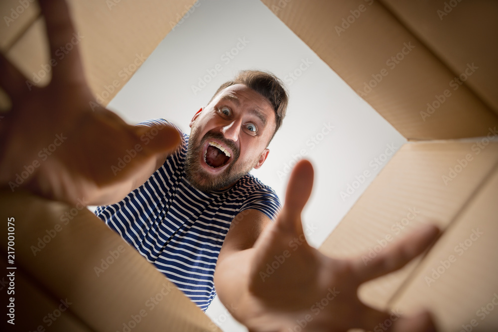 The surprised man unpacking, opening carton box and looking inside. The ...