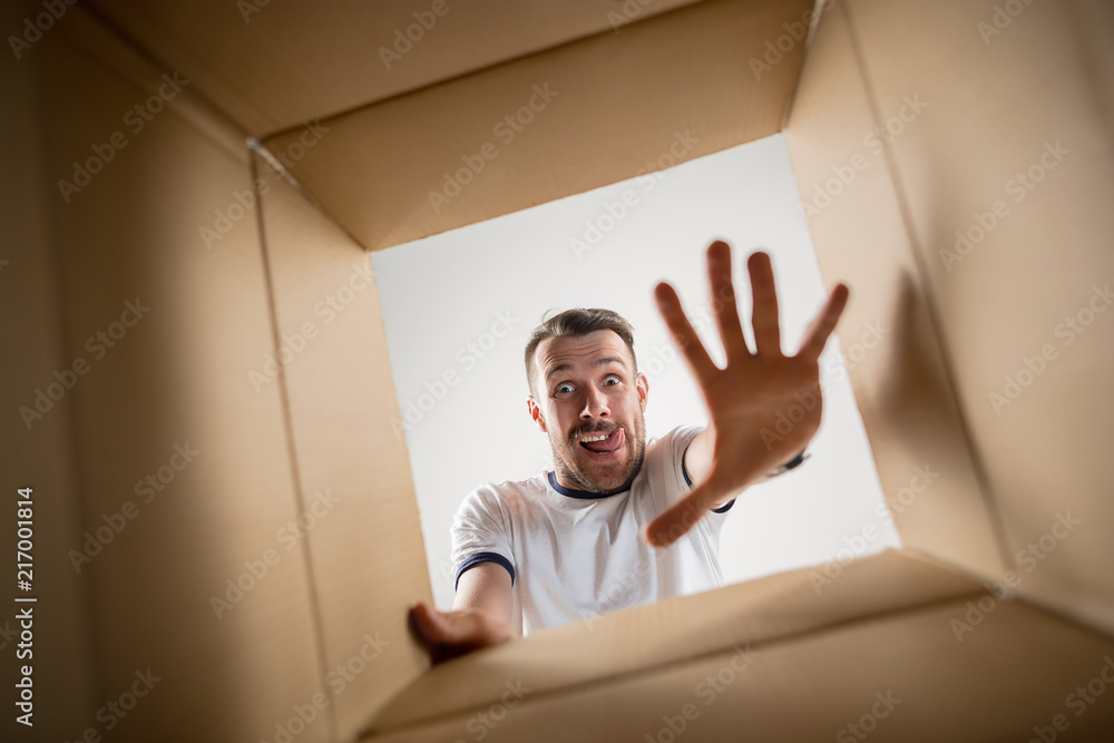 The surprised man unpacking, opening carton box and looking inside. The ...