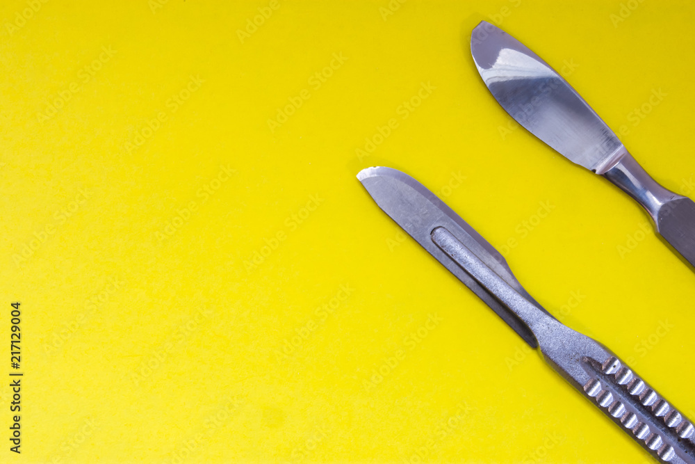 Two metal chrome surgical scalpel are on a yellow background with space ...