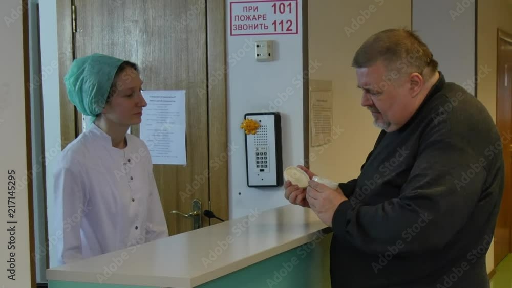 Nurse takes medical card from fat man in clinic. Girl in white lab coat ...