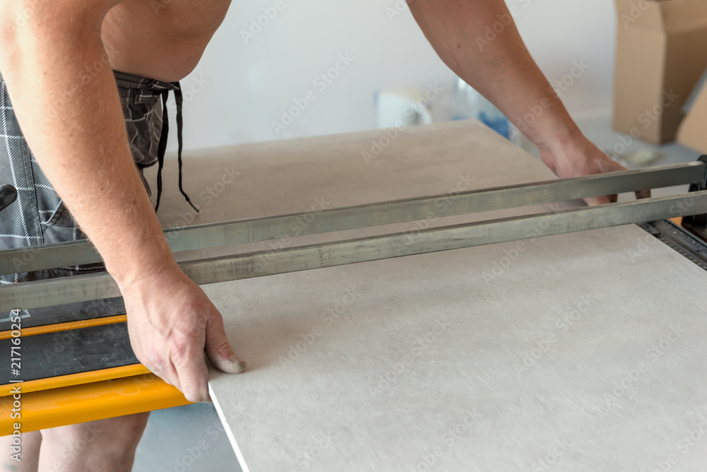 The man is cutting the floor tiles using a tile cutter machine. Stock ...