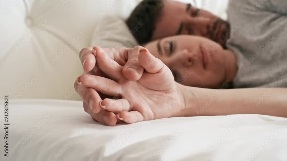 Handheld PAN of bearded man lying with closed eyes in bed and hugging ...