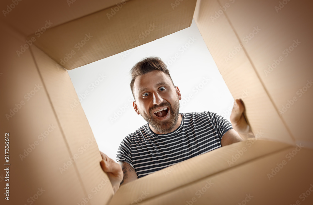 The surprised man unpacking, opening carton box and looking inside. The ...