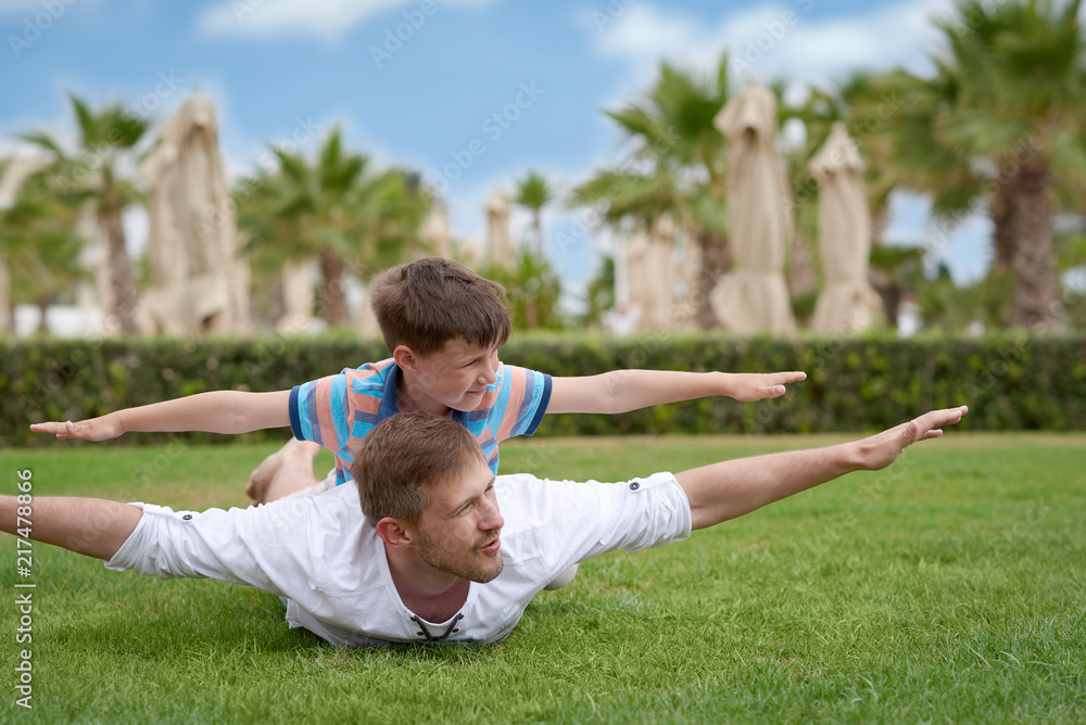 Father and son flying like planes at the lawn of the resort territory ...
