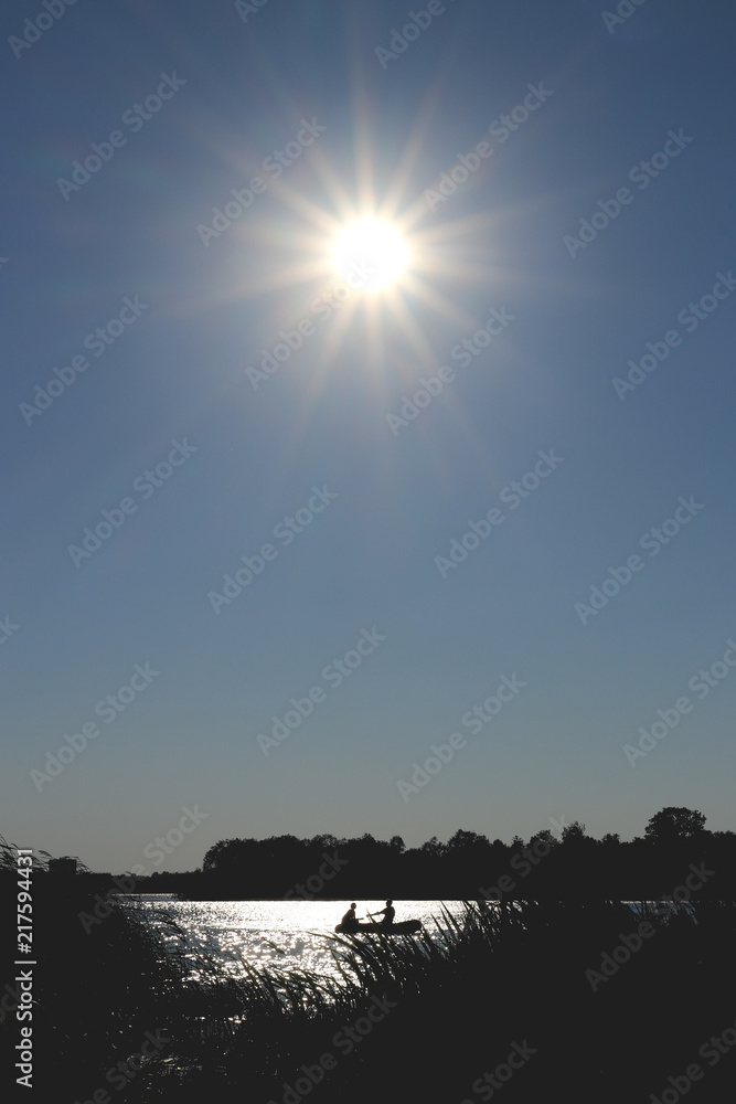 Silhouettes of two people on a rubber boat in a sunny reflection & cane ...