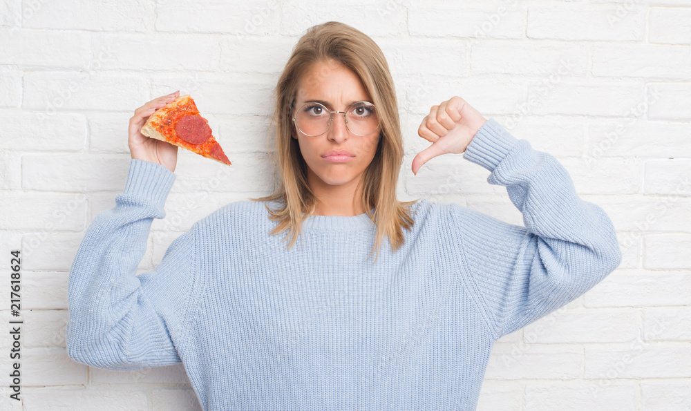 Foto de Beautiful young woman over white brick wall eating pizza slice ...