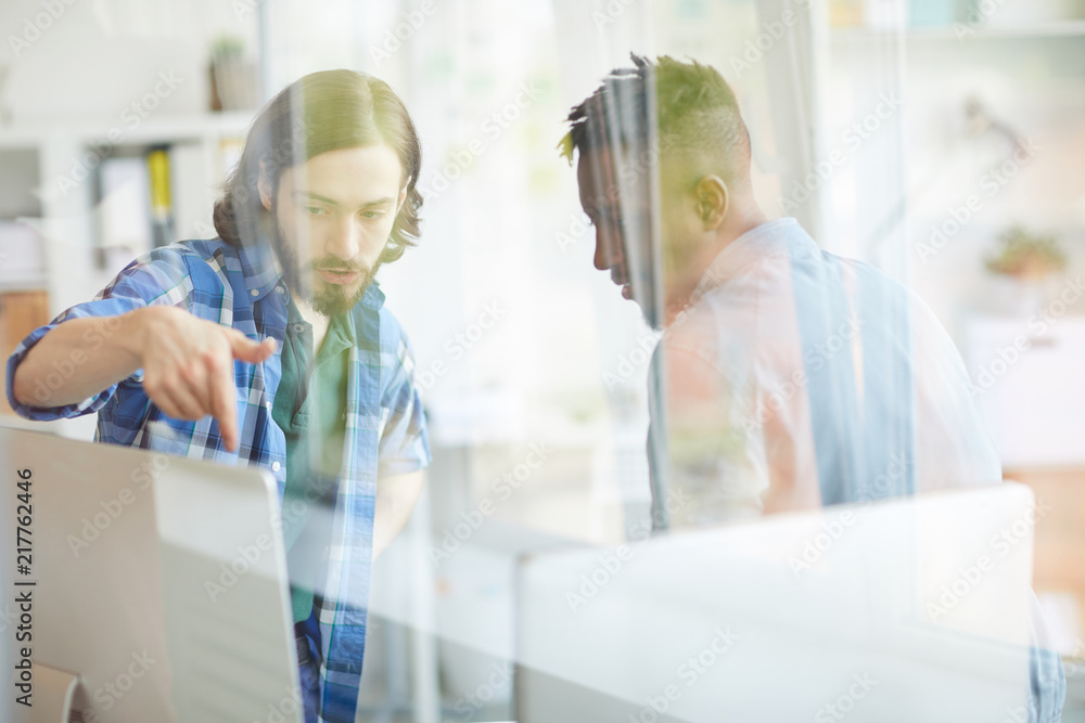 One of young it specialists pointing at computer monitor while ...