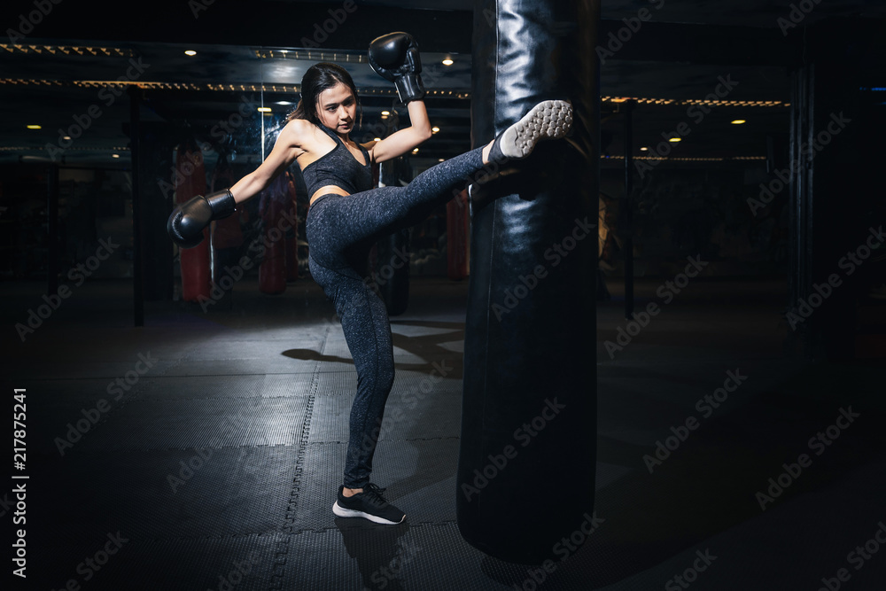 Female boxer hitting a huge punching bag at a boxing studio. Woman boxer training hard. Thai ...