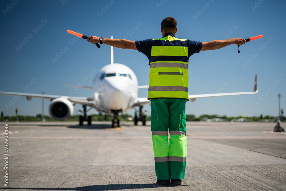 Welcome back. Back view of airport worker looking at passenger plane ...