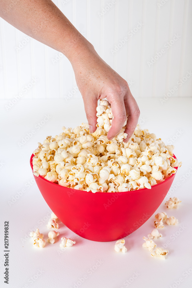 Vertical of hand reaching for popped popcorn in a big red plastic bowl ...