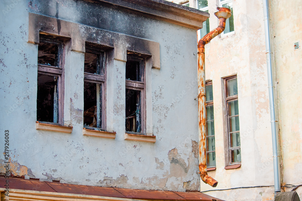 The facade of a burnt building with a rusty drainpipe and peeling walls ...