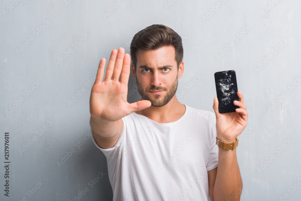 Handsome young man over grey grunge wall showing broken smartphone ...