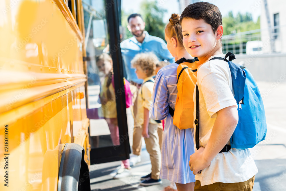 little schoolboy entering school bus with classmates while teacher ...