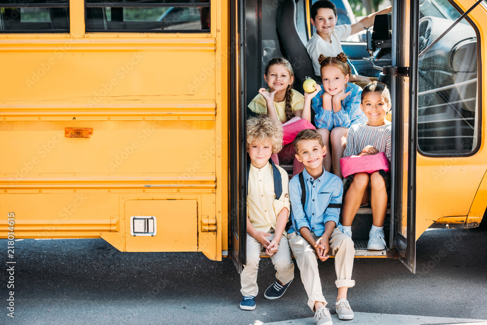 group of adorable schoolchildren sitting on stairs of school bus and ...